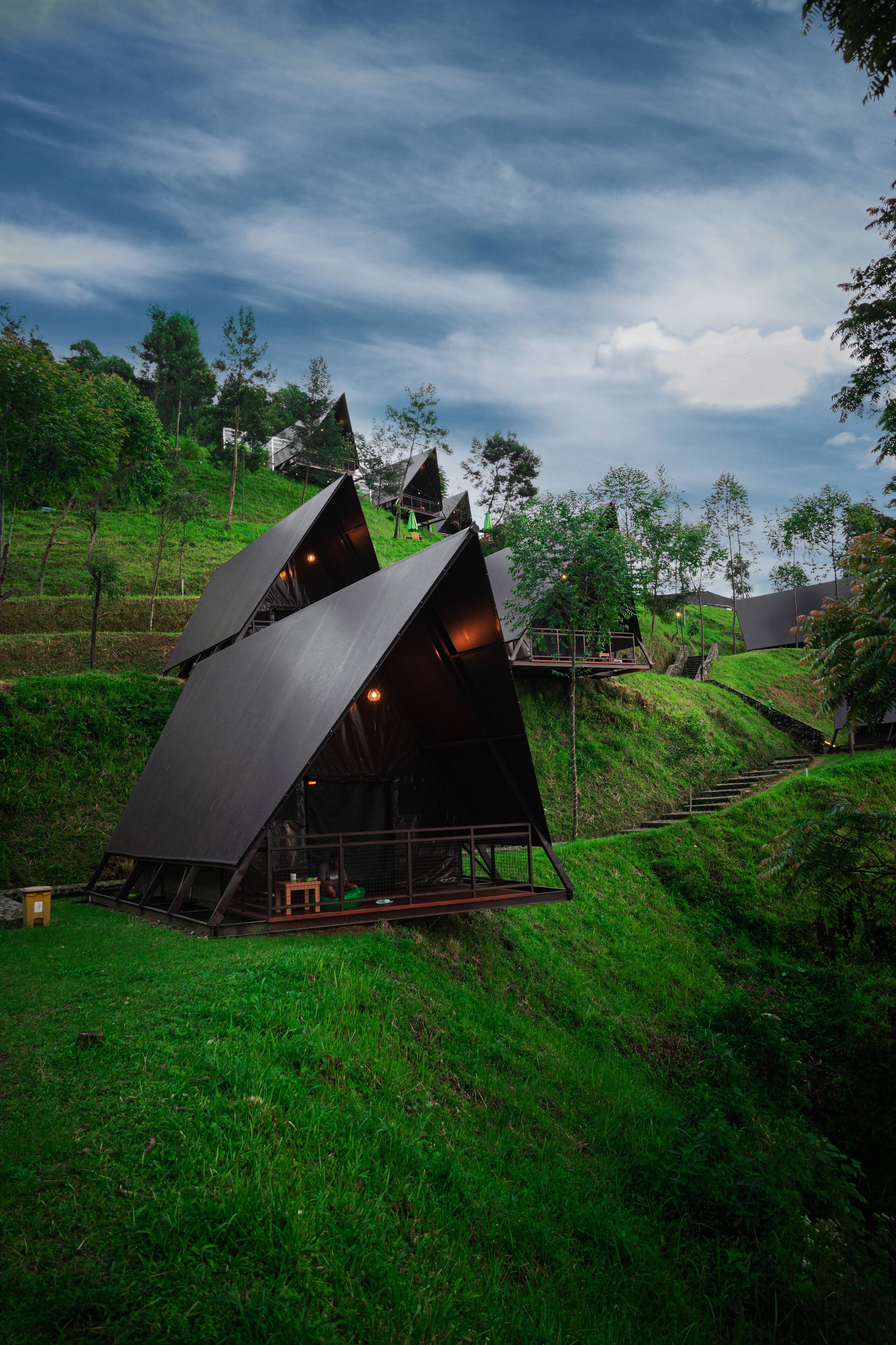 Um edifício moderno de formato triangular com telhado plano, localizado numa encosta gramada.