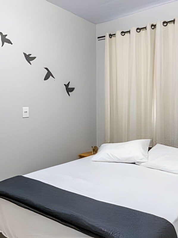 Quarto com cama, cortinas brancas e decorações de pássaros nas paredes.