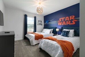 Quarto de hotel com tema Star Wars, com duas camas, um guarda-roupa, uma secretária e um poster de Star Wars na parede.
