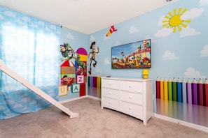 Um quarto infantil com escorrega, blocos do alfabeto, cômoda branca, parede de lápis coloridos e pintura de montanha-russa.