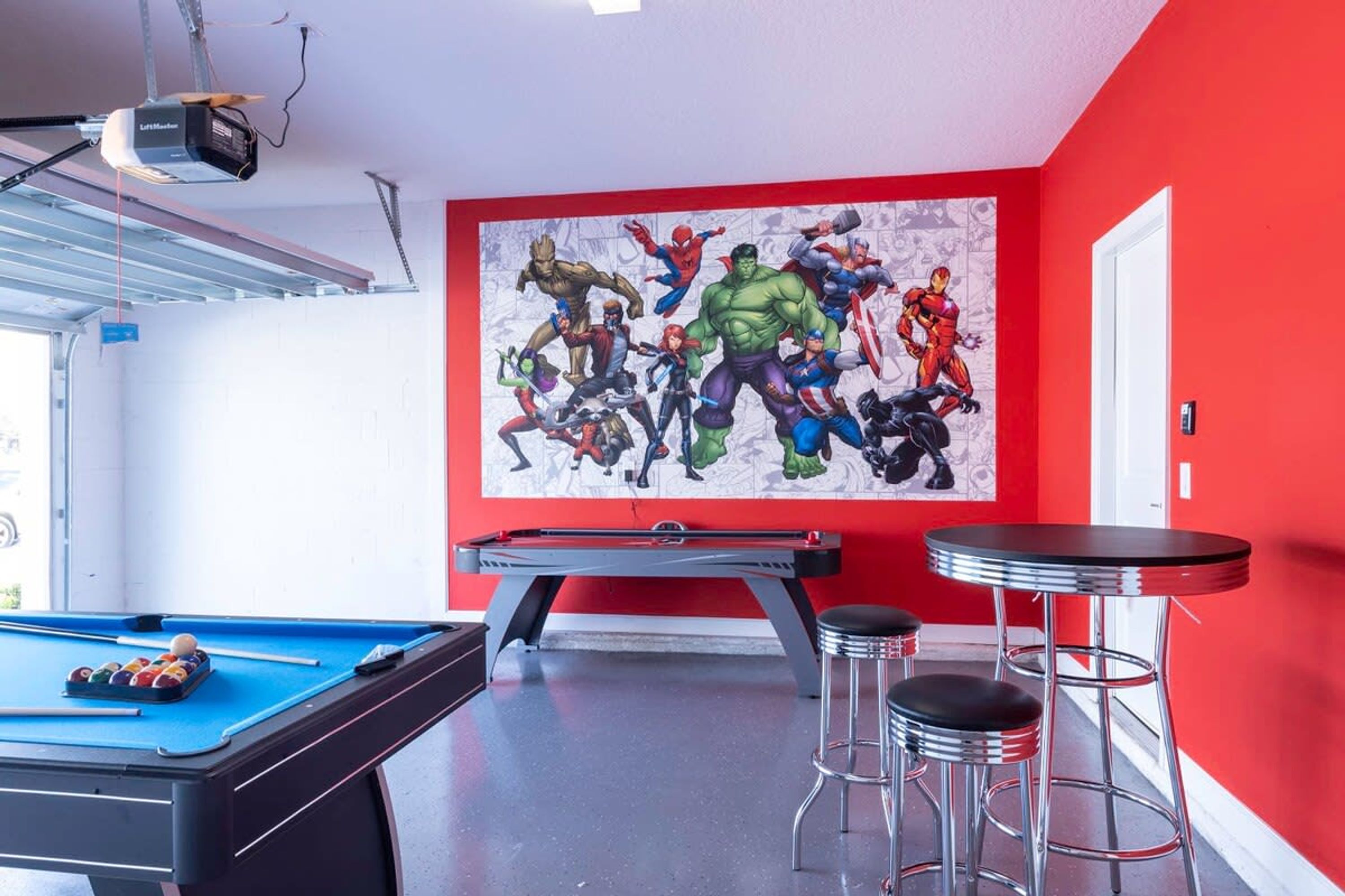 Quarto com mesa de bilhar, projetor e um mural de super-heróis na parede.