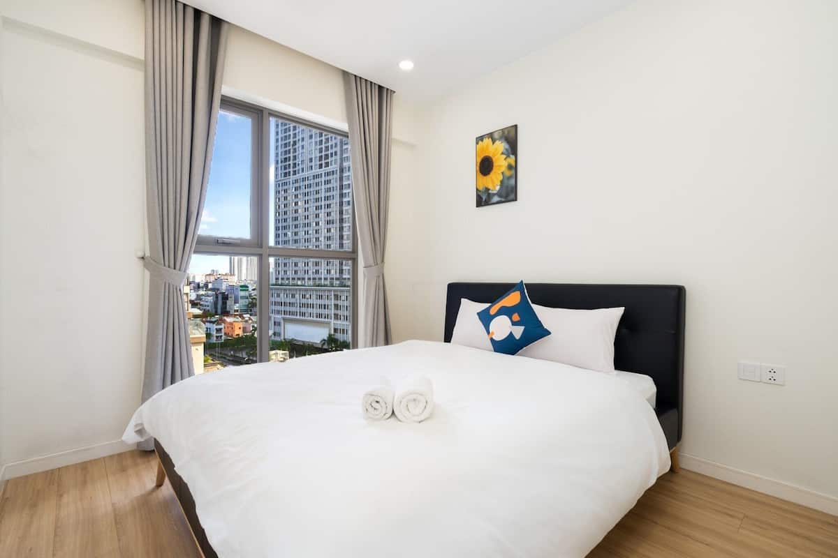 Quarto de hotel com uma cama grande, vista para a cidade através da janela e um quadro de girassol na parede.