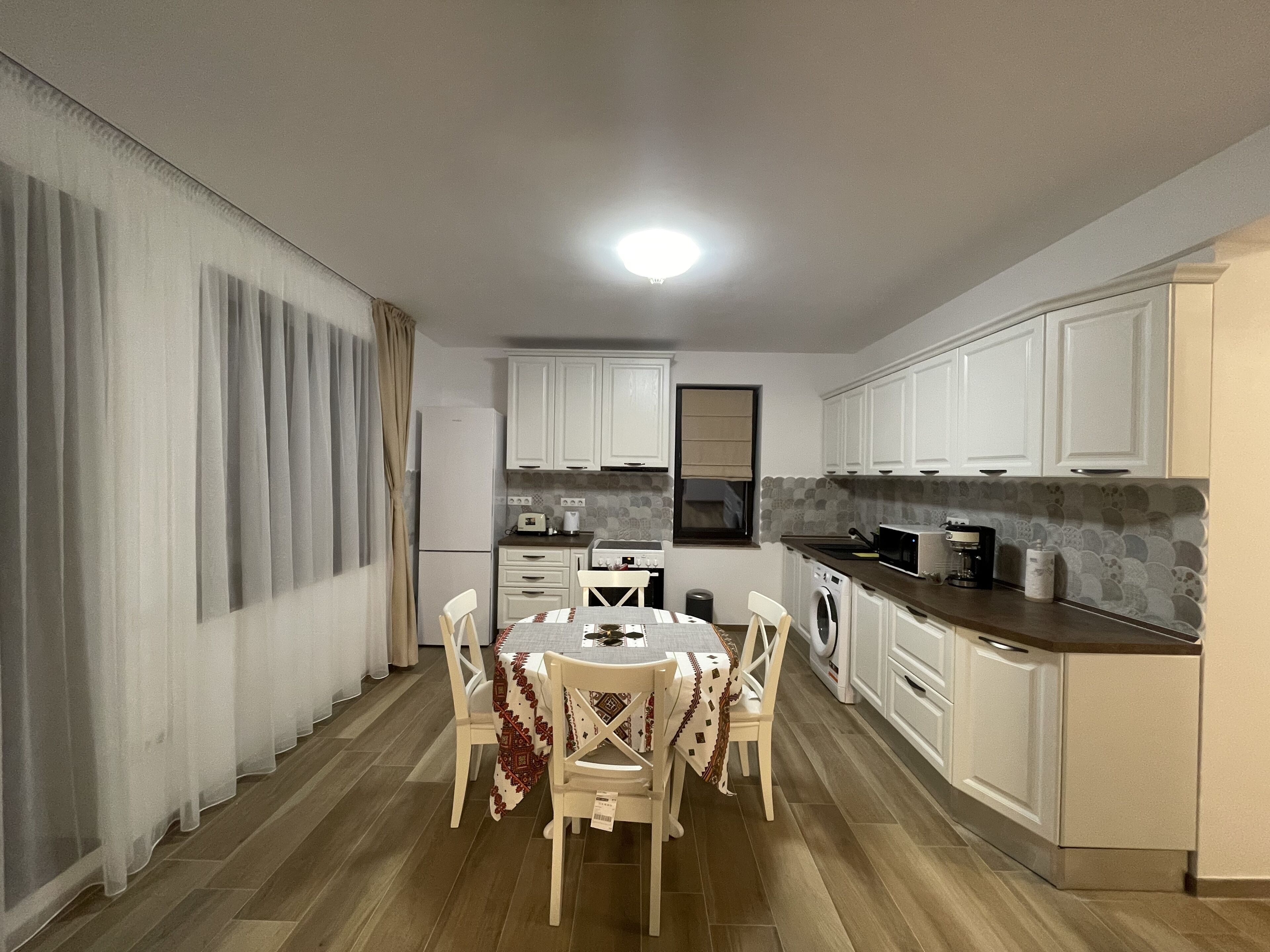 Cozinha compacta com armários brancos, mesa de jantar com cadeiras, forno embutido e micro-ondas.