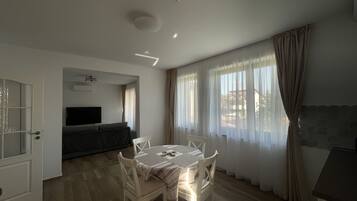 Uma sala de estar ampla com uma mesa de jantar, cadeiras, um sofá e uma televisão.