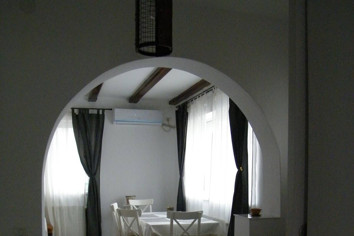Uma área de refeições com mesa e cadeiras brancas, uma porta em arco e um lustre.