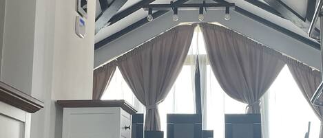 Quarto espaçoso com pé-direito alto, grandes janelas com cortinas e um espaço de estar moderno.