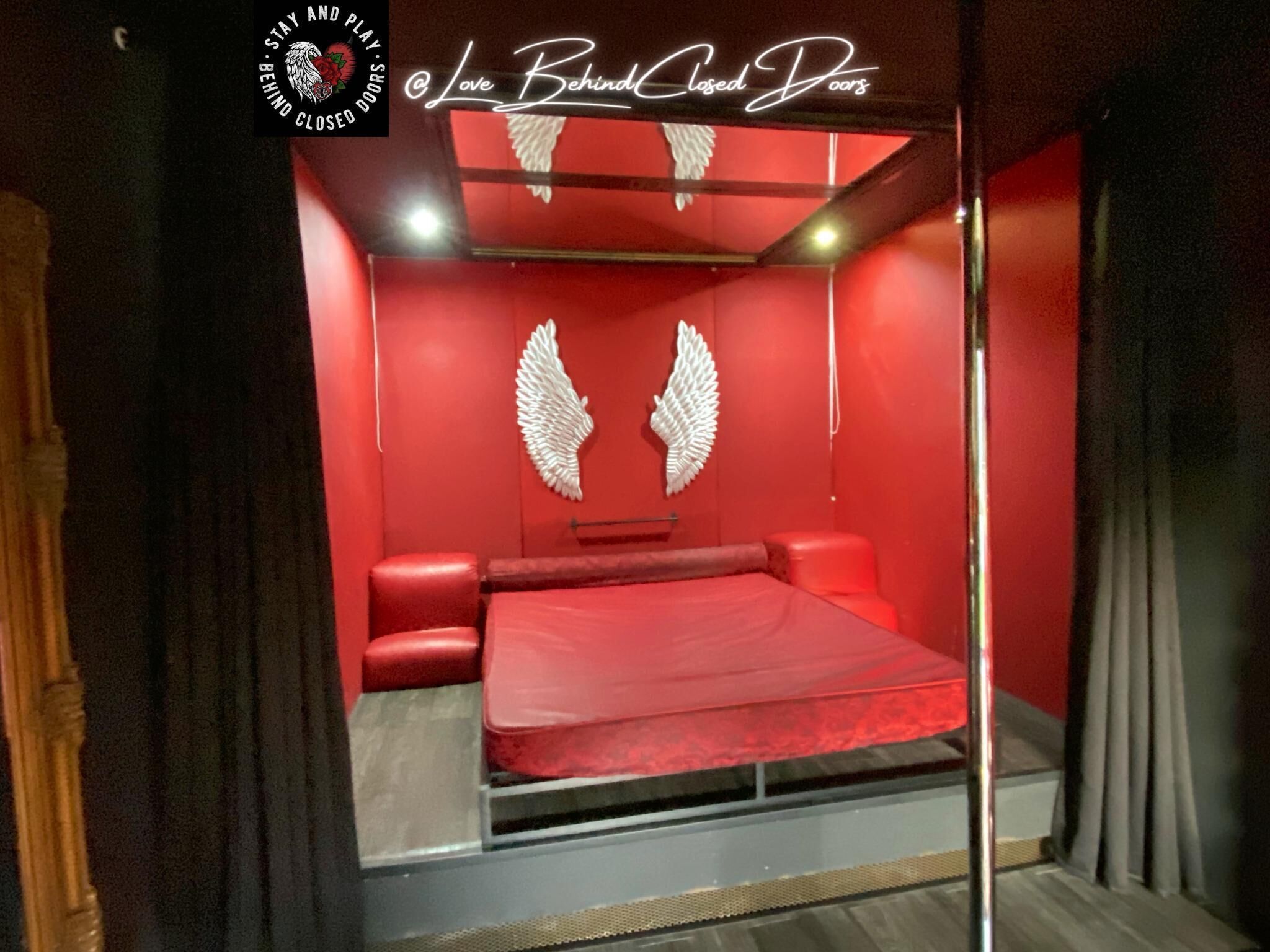Quarto com decoração em tons de vermelho, com uma cama, duas poltronas vermelhas e detalhes decorativos brancos em formato de asas na parede.