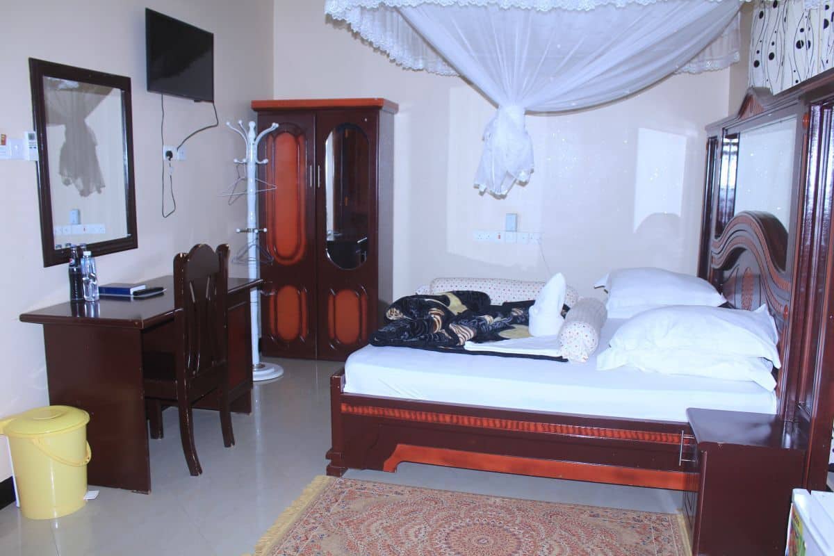 Quarto com cama, escrivaninha, cadeira, guarda-roupa, espelho e televisão.