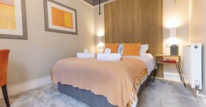 Quarto de hotel bem arrumado, com uma cama, mesa de cabeceira, cadeira e radiador.