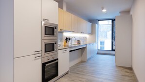 Cozinha moderna com eletrodomésticos embutidos, uma janela ampla e vista para um edifício.