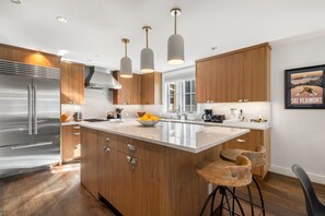 Cozinha moderna com armários de madeira, eletrodomésticos de aço inoxidável e iluminação pendente.