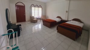 Quarto de hotel com duas camas, uma cadeira, uma escrivaninha e um espelho.