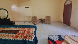 Quarto com cama, duas cadeiras, uma mesa pequena, espelho e porta.