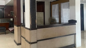 Um hall amplo com balcão de atendimento, um ventilador e uma janela com cortinas.