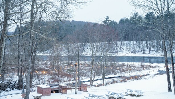 Uma área externa coberta de neve, com mesas de piquenique e estruturas de tijolo, provavelmente um camping ou parque.