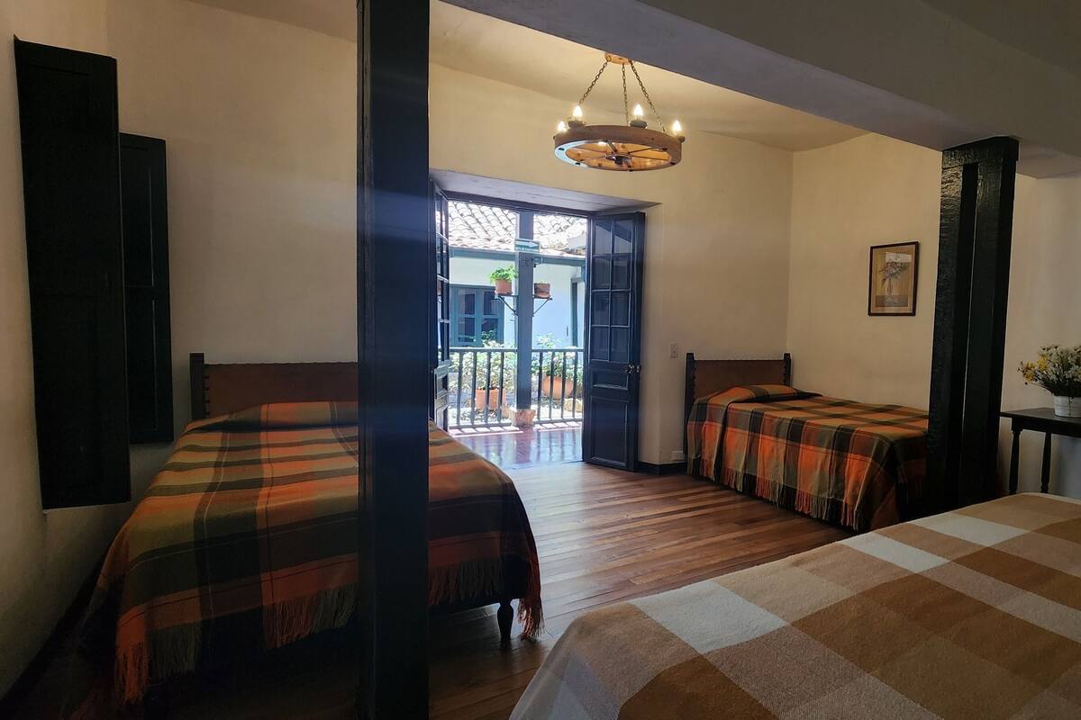 Quarto de hotel com duas camas, um guarda-roupa de madeira grande, um candelabro e uma varanda com plantas em vasos.