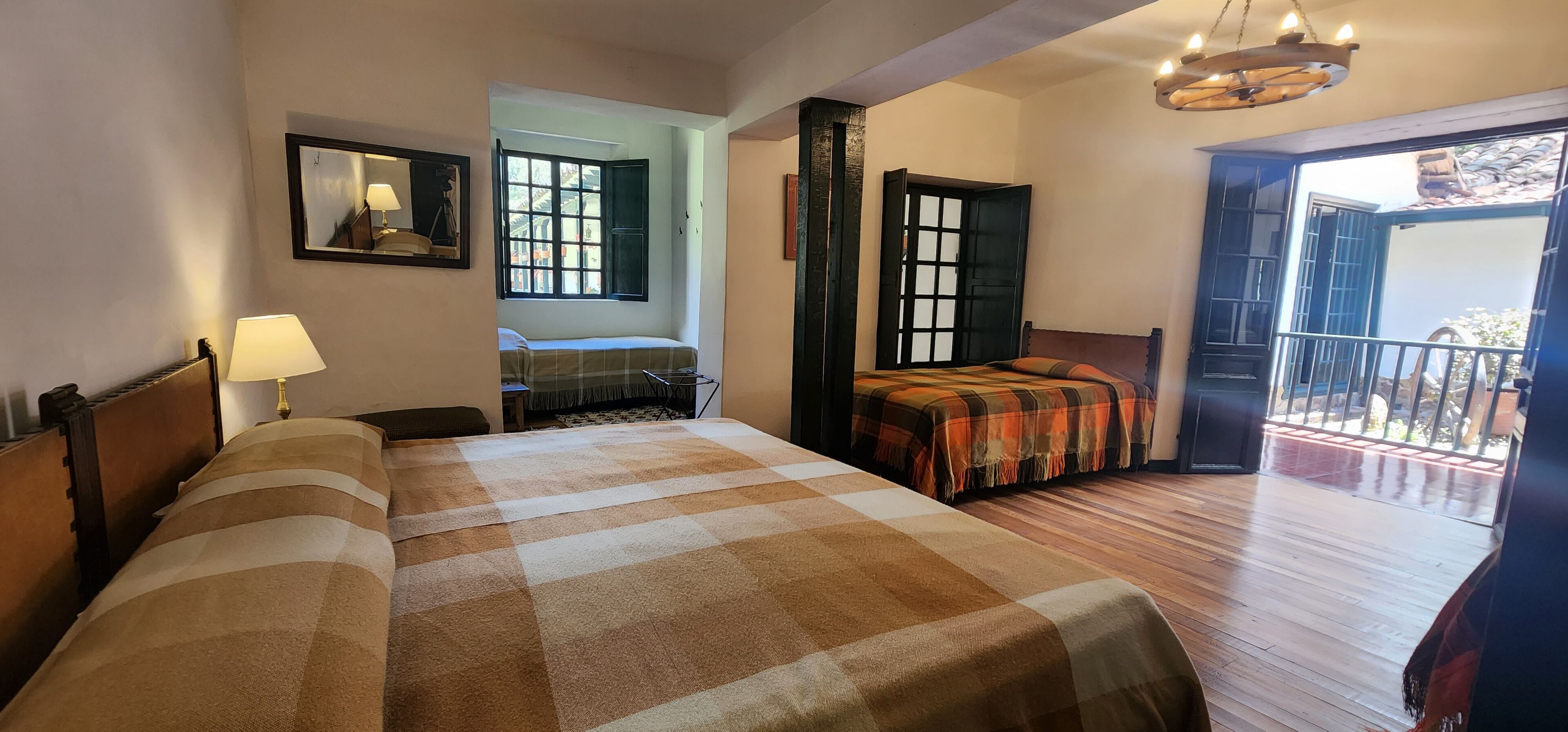 Quarto de hotel com duas camas, varanda, piso de madeira e uma janela grande com persianas.