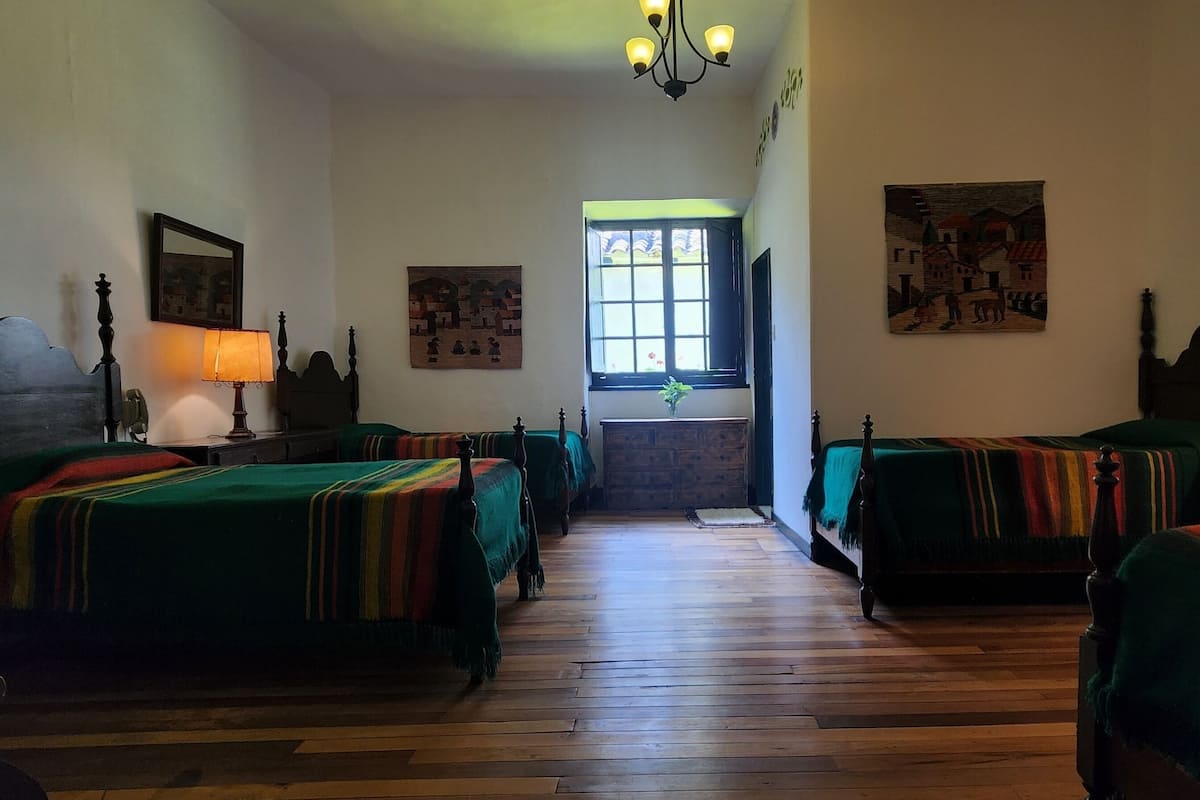 Quarto de hotel com quatro camas de solteiro, piso de madeira, um candelabro e obras de arte nas paredes.