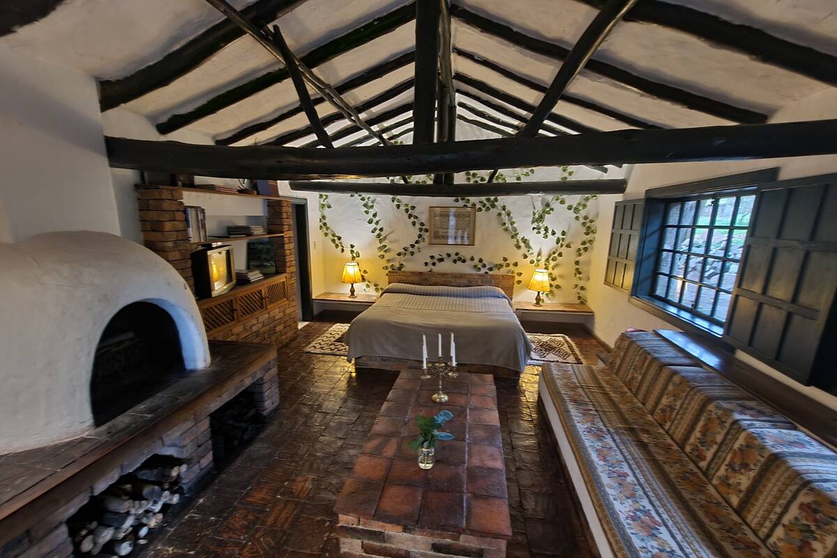 Um quarto rústico com lareira de tijolos, uma cama, um banco e uma janela com vista.