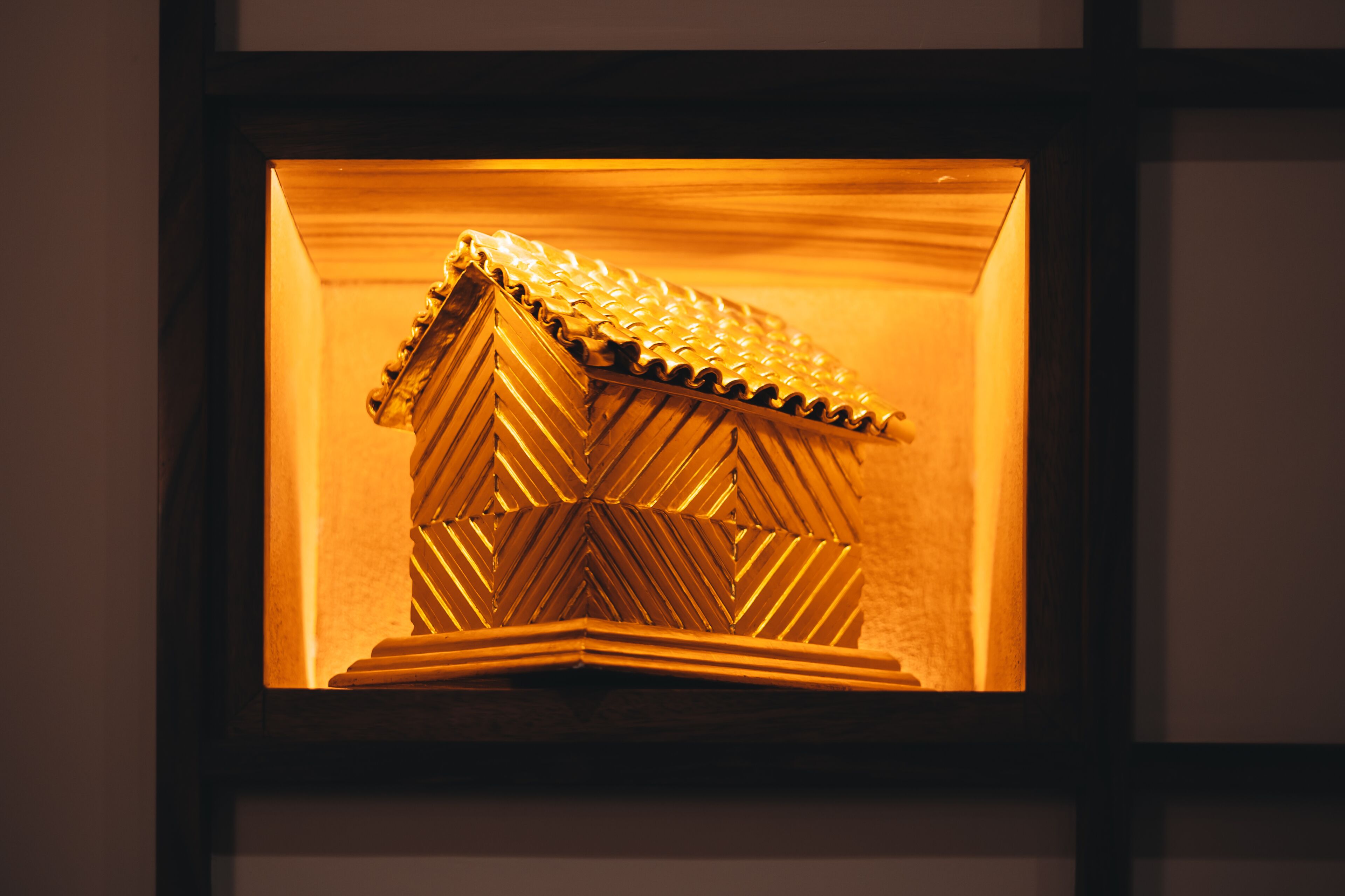 Modelo arquitetônico emoldurado de uma casa com telhado triangular e fachada em padrão de losangos.