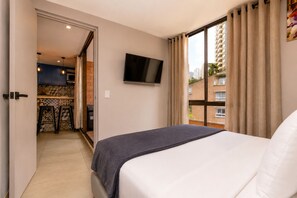 Quarto de hotel com cama, televisão, vista da cidade e cozinha compacta.