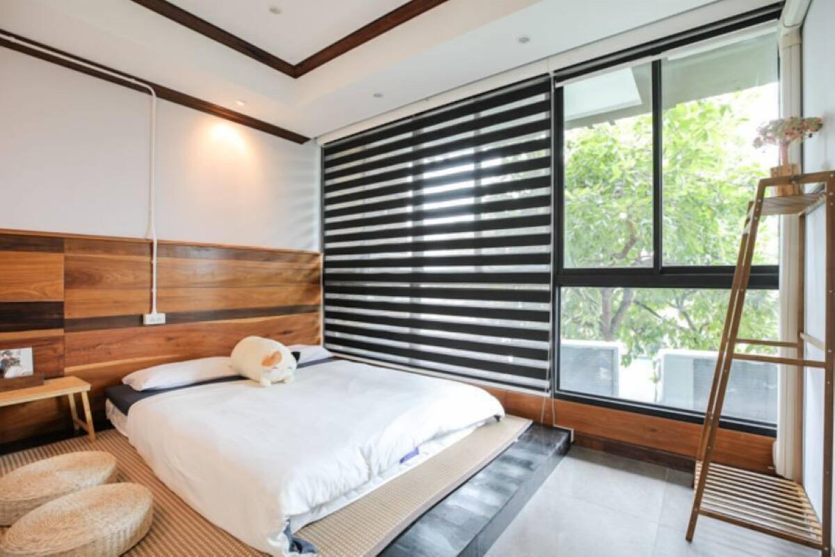 Um quarto moderno com uma janela grande, uma cabeceira de madeira, uma cama com roupa de cama branca, uma mesa de cabeceira e uma escada encostada na parede.
