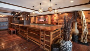 Uma área de bar com banquetas de madeira, uma grande pintura de peixe e luminárias pendentes.