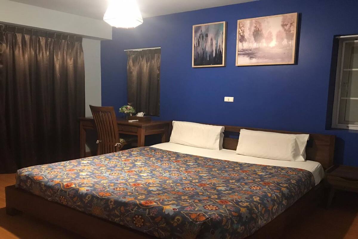Quarto com uma cama grande, uma escrivaninha e duas pinturas na parede.
