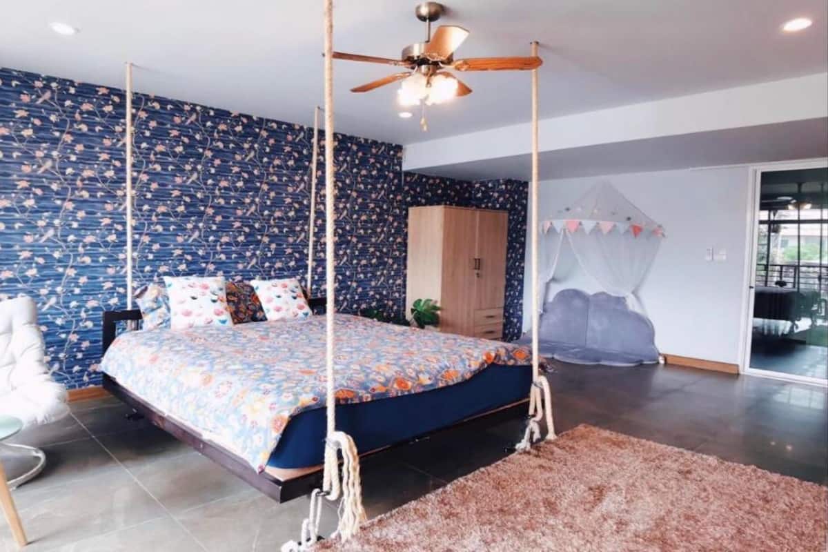 Quarto com cama de dossel, poltrona branca, mesinha e uma janela grande.
