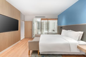 Quarto de hotel moderno com cama, mesa de cabeceira e TV fixada na parede.