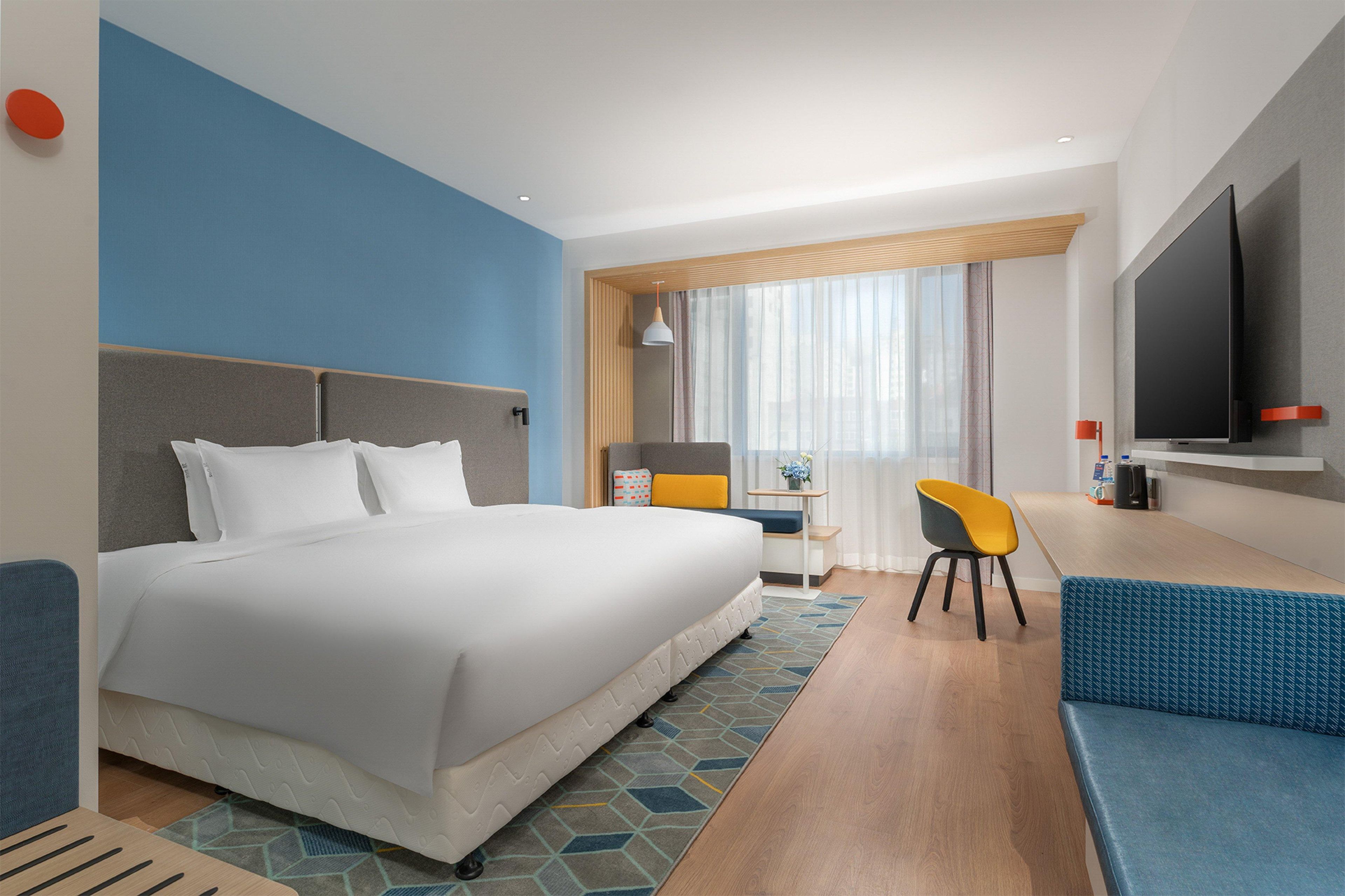Quarto de hotel com uma cama grande, uma escrivaninha com cadeira, uma televisão e um sofá.