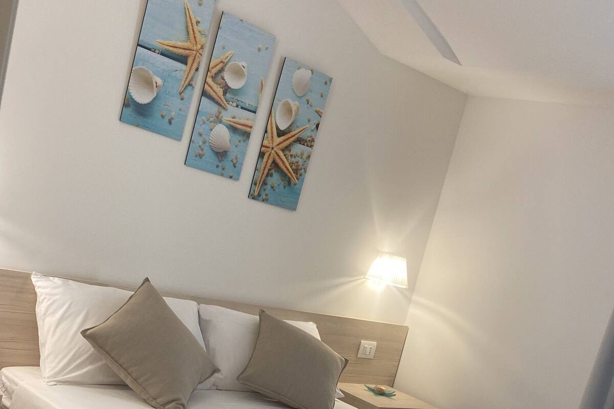 Quarto com cama, almofadas, mesa de cabeceira e um painel decorado com arte de estrelas-do-mar.