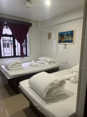 Quarto de hotel com duas camas, janela com cortinas, um quadro na parede e um ventilador de teto.