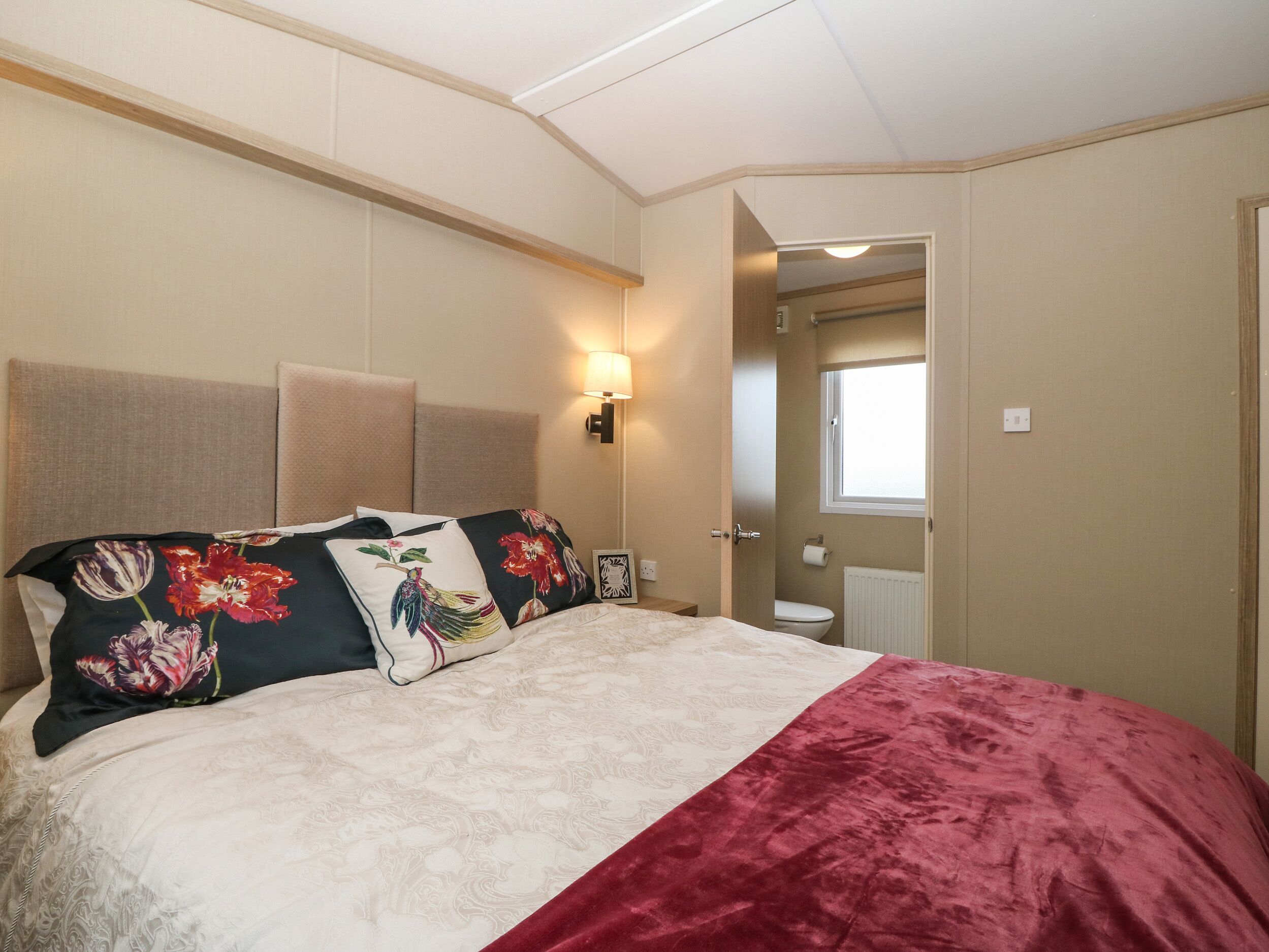 Quarto com uma cama grande, uma mesa de cabeceira, um abajur fixado na parede e uma porta que dá para o banheiro.