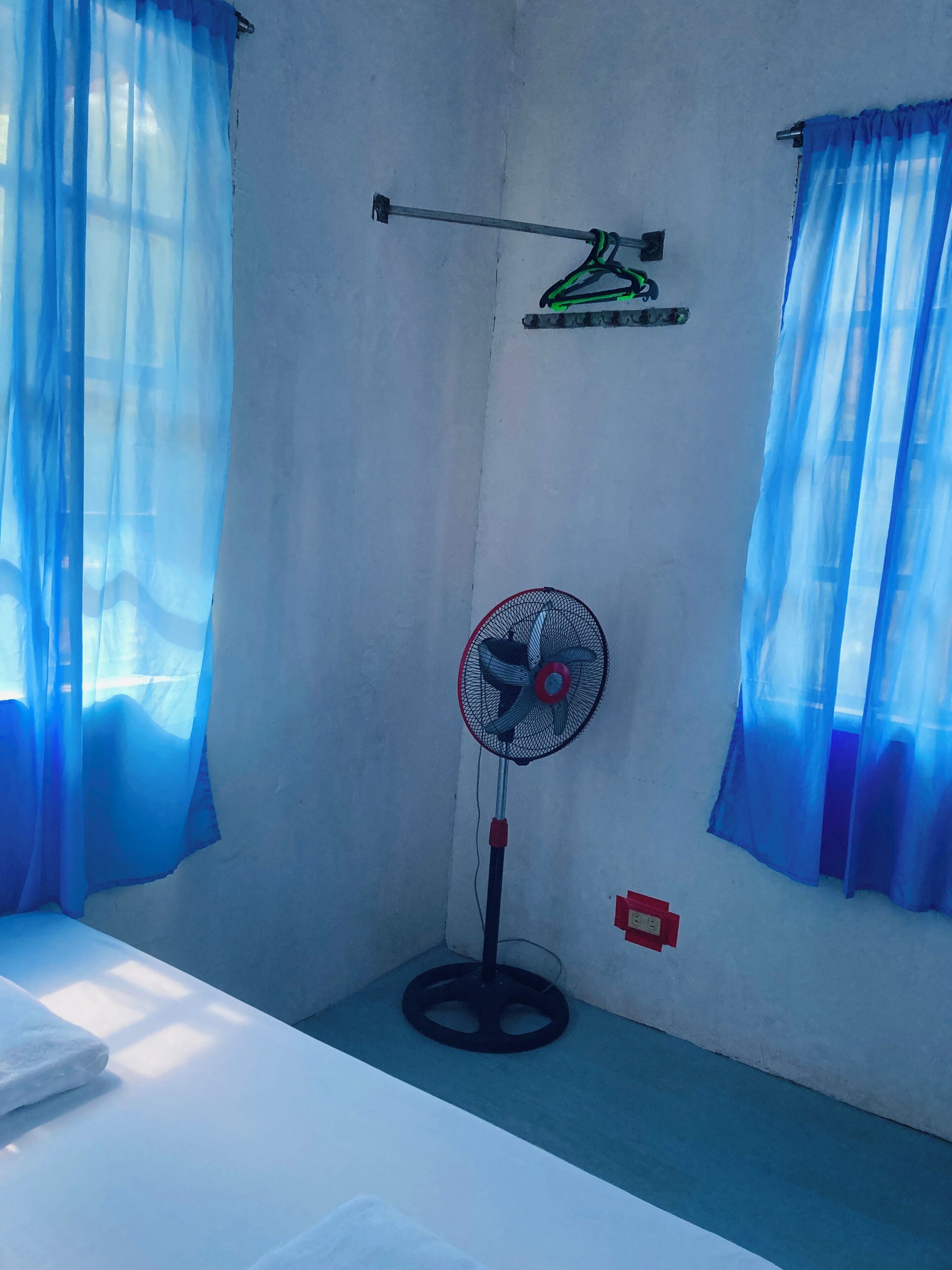 Quarto com uma cama, um ventilador e uma prateleira com um objeto verde.