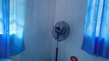 Quarto com uma cama, um ventilador e uma prateleira com um objeto verde.