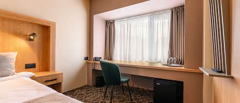 Quarto de hotel com cama, escrivaninha, cadeira e janela com cortinas.