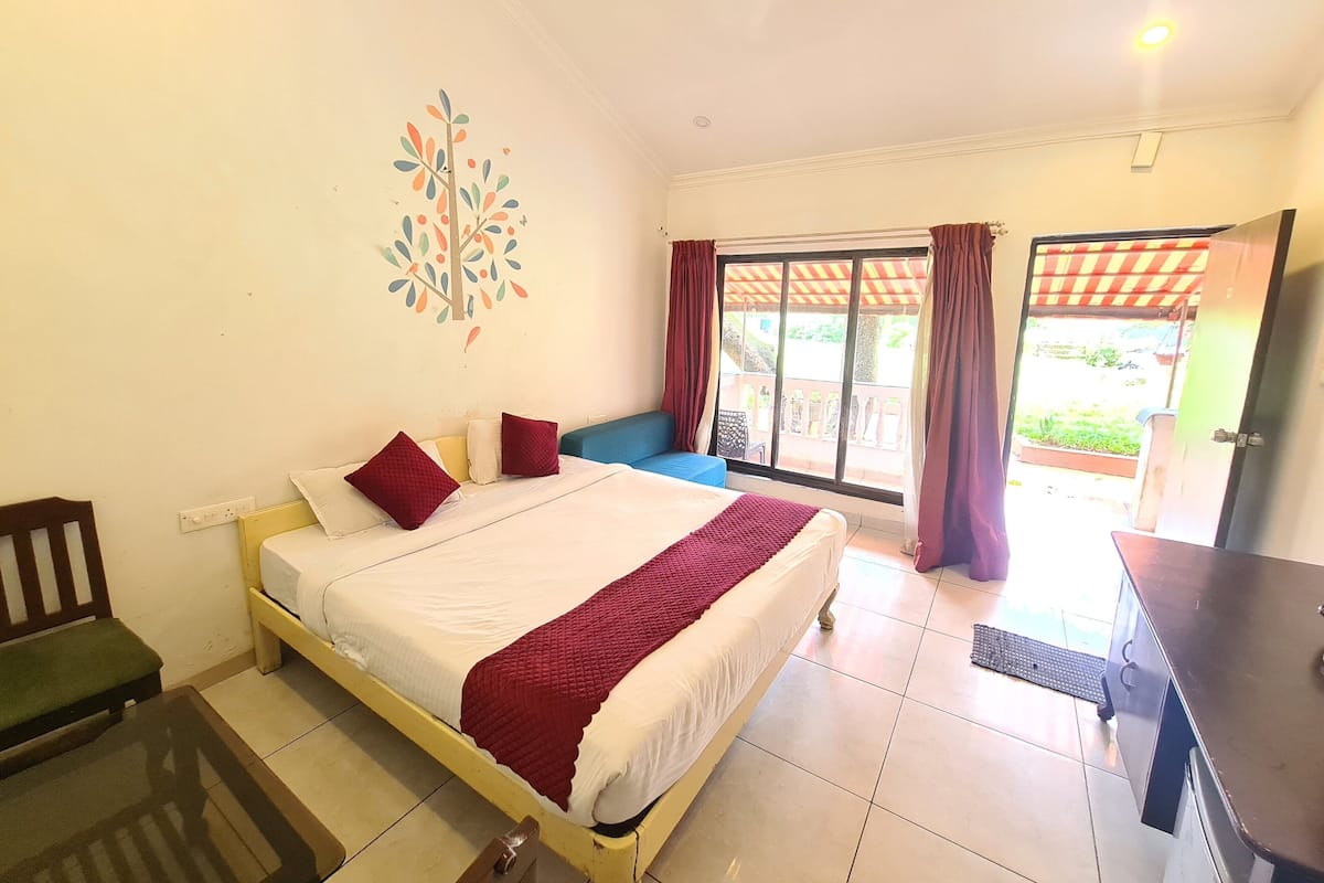 Quarto de hotel com cama, escrivaninha, cadeira e vista para o exterior através de uma porta deslizante.