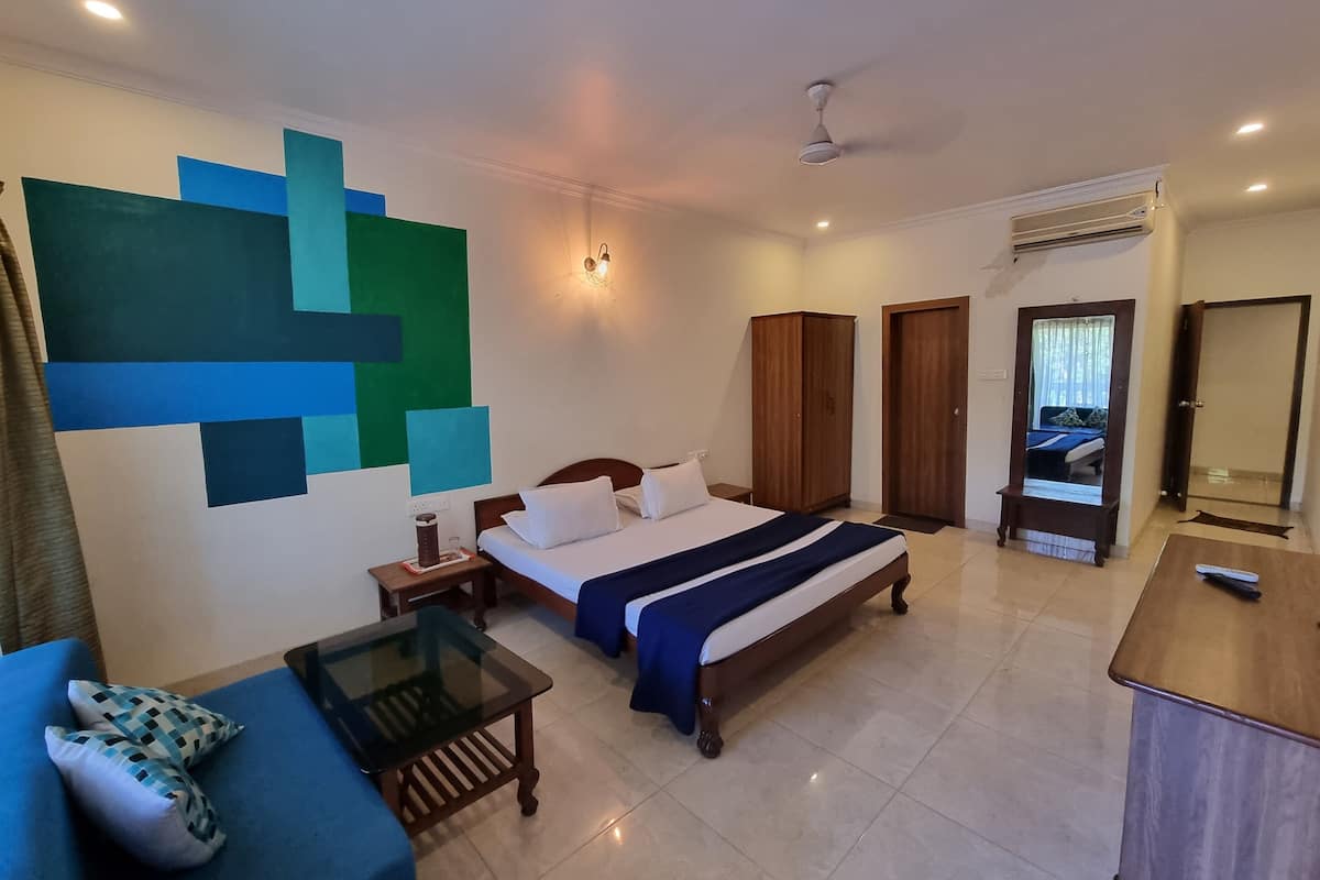 Quarto de hotel com cama, escrivaninha, cadeira e uma grande obra de arte abstrata na parede.