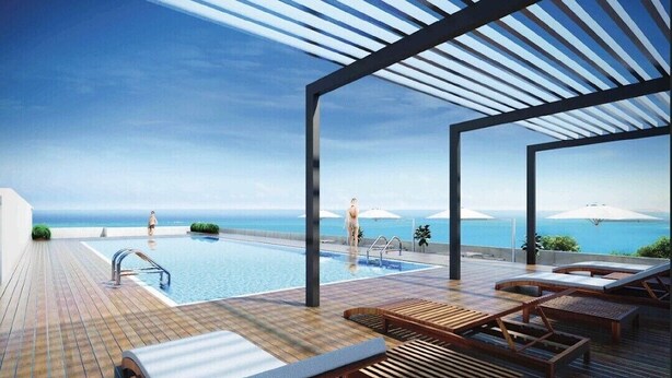 Uma área de piscina no terraço com espreguiçadeiras de madeira e vista para o oceano.