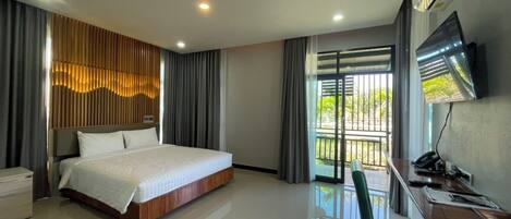 Quarto de hotel moderno com uma cama grande, uma mesa com cadeira, televisão e uma varanda com vista para o verde.