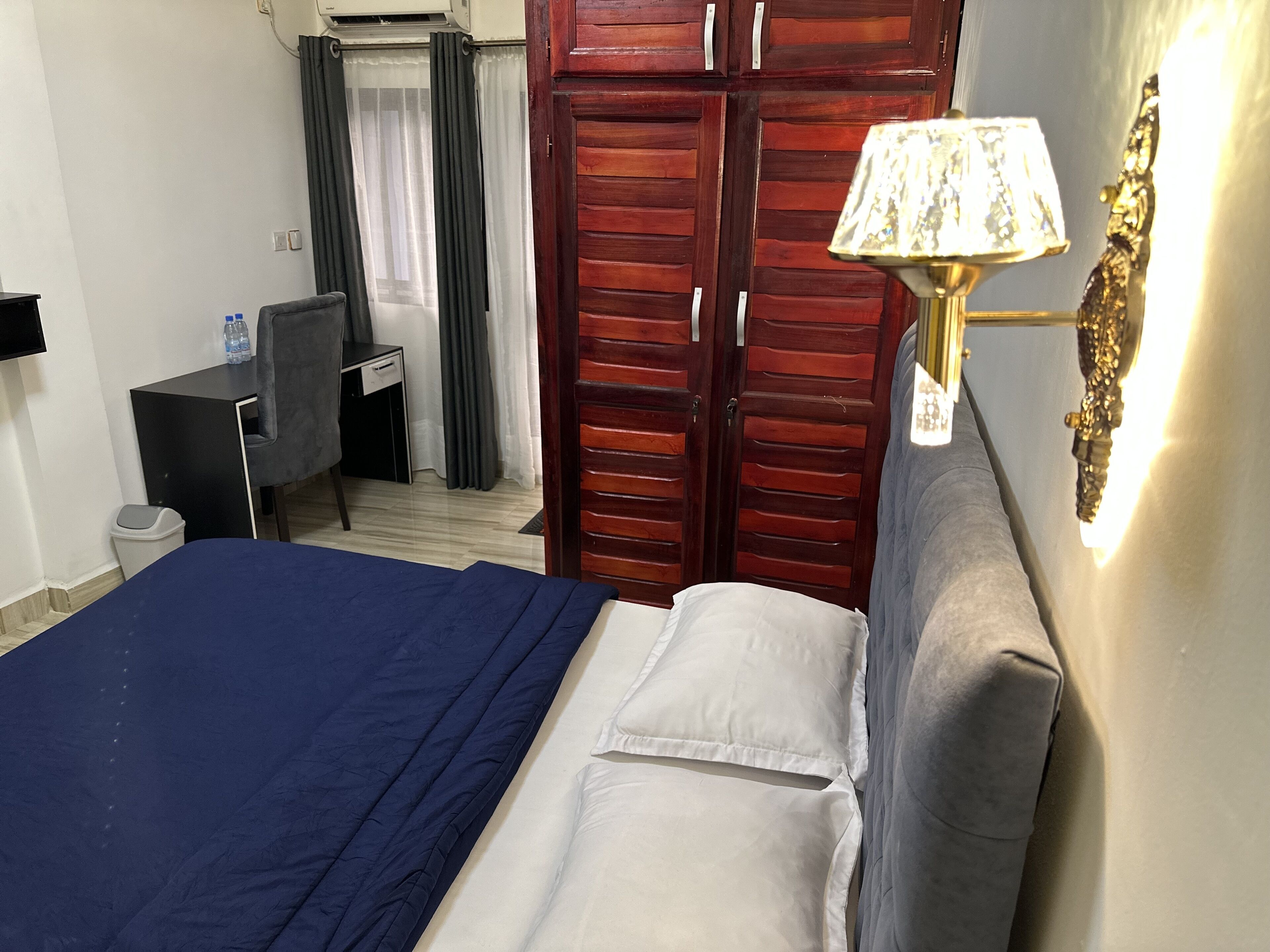 Quarto de hotel com cama, escrivaninha, cadeira, guarda-roupa e abajur.