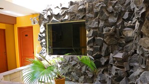 Uma parede de pedra com uma janela, uma planta em vaso e uma porta com placa de número.