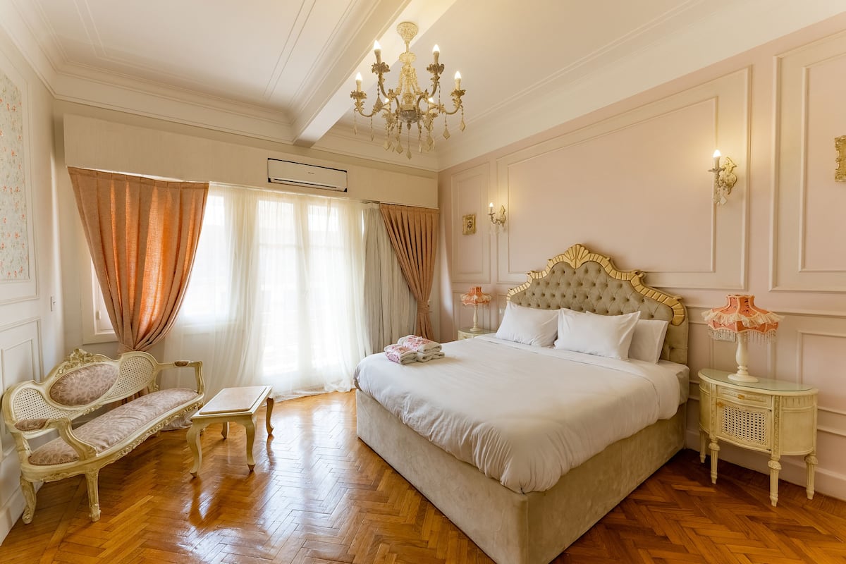 Quarto com uma cama grande, um chaise longue, uma mesinha e um candelabro.