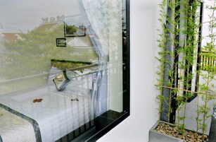 Um interior moderno com uma grande janela refletindo uma cena de rua, um pequeno jardim interno com bambu e uma parede branca.