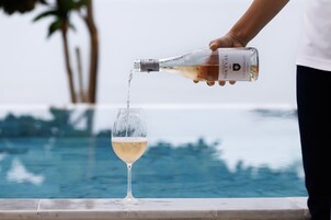 Alguém servindo vinho de uma garrafa em um copo perto de uma piscina.