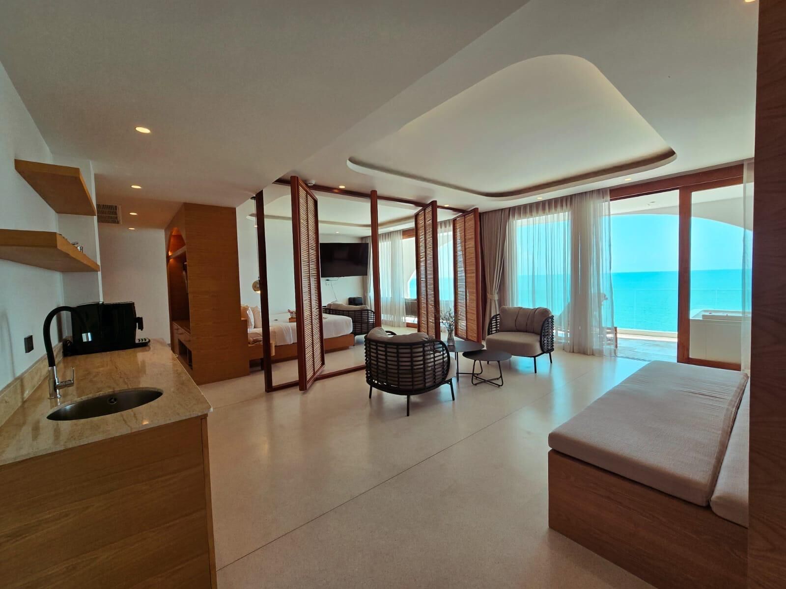 Quarto de hotel moderno com uma cama grande, sofá, máquina de café e vista para o mar.