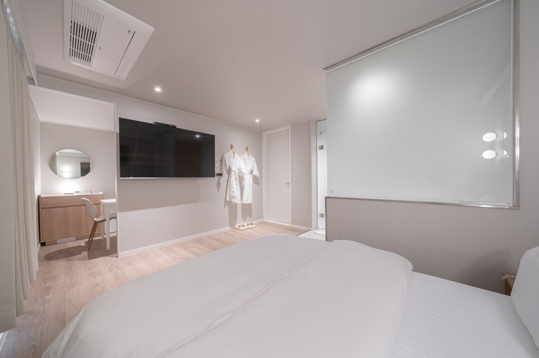 Quarto de hotel moderno com uma cama grande, televisão de tela plana, espelho e pequena escrivaninha com cadeira.