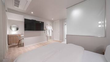 Quarto de hotel moderno com uma cama grande, televisão de tela plana, espelho e pequena escrivaninha com cadeira.