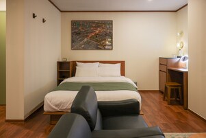Quarto com cama, mesa de cabeceira, cadeira, escrivaninha e um quadro na parede.